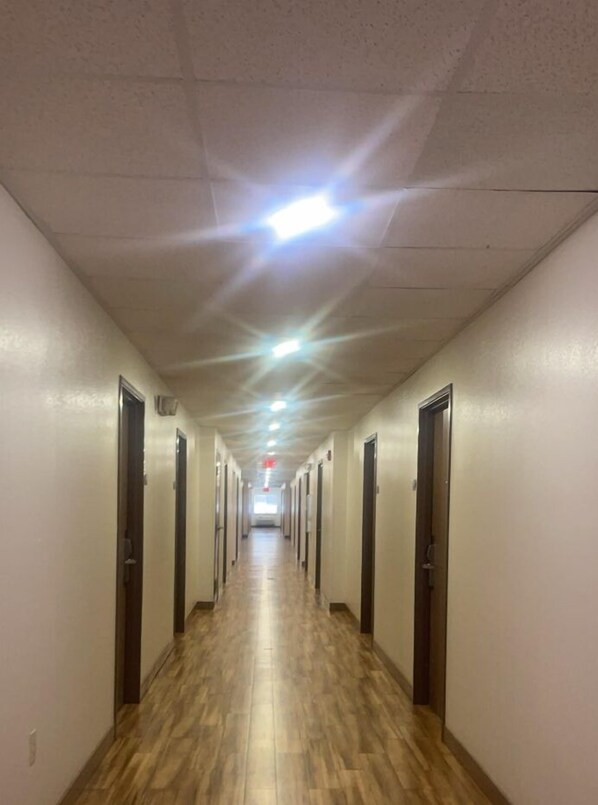 Corredor longo e estreito de hotel, com assoalho de madeira e portas em ambos os lados.