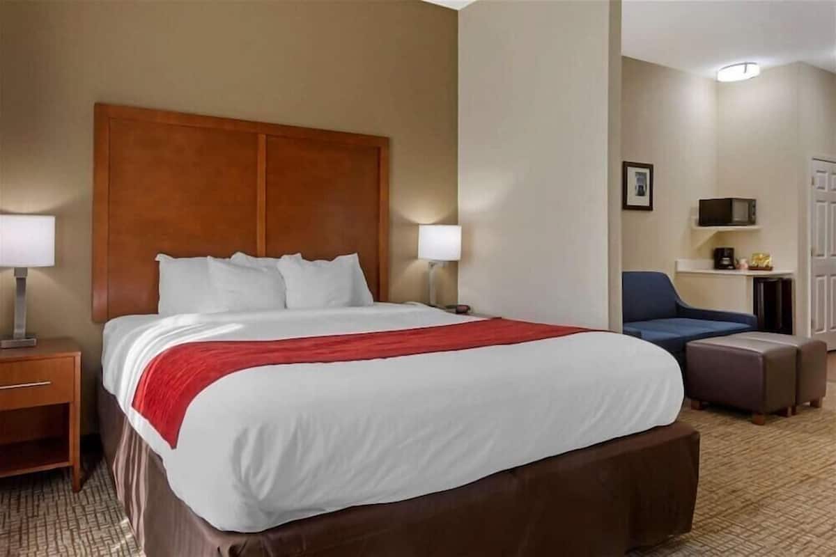 Quarto de hotel com uma cama grande, duas luminárias de cabeceira, uma escrivaninha com cadeira e um micro-ondas na parede.