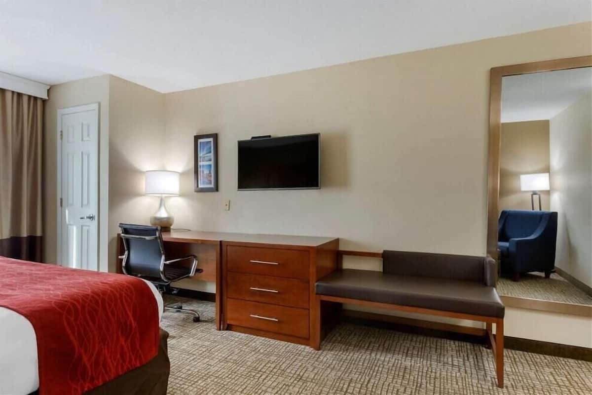 Quarto de hotel com cama, escrivaninha, cadeira e televisão.
