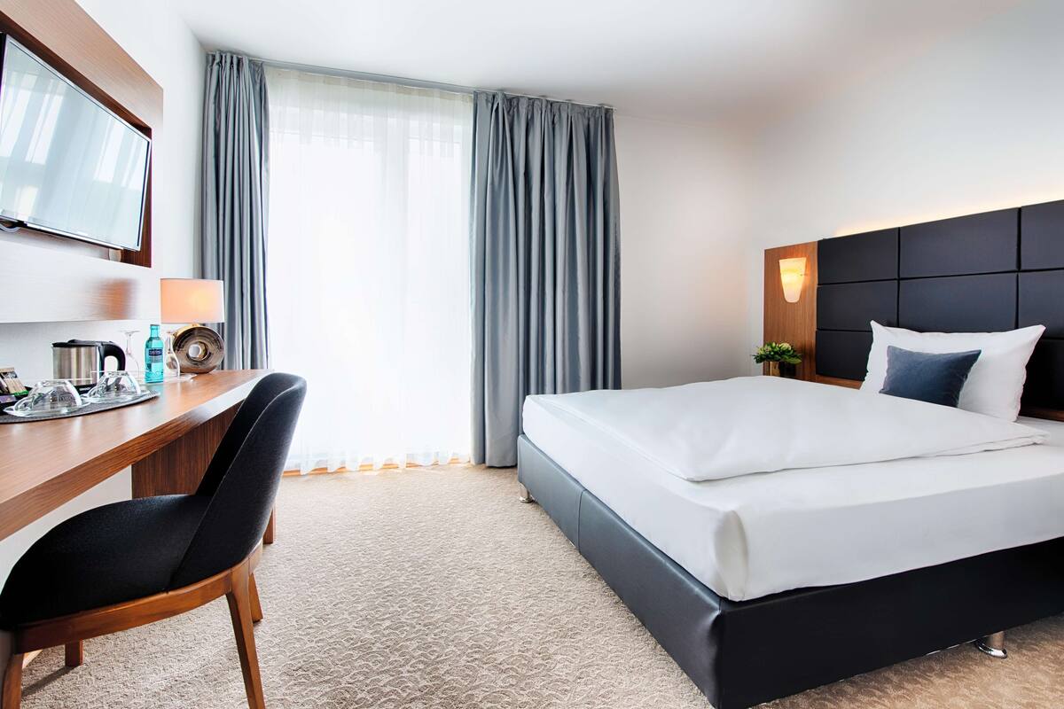 Quarto de hotel com cama, escrivaninha, cadeira e televisão.