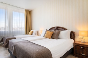 Quarto de hotel com duas camas, uma mesinha de cabeceira e uma janela com cortinas.