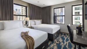 Quarto de hotel com duas camas, uma mesa de jantar com cadeiras, vista para a cidade e um minibar.