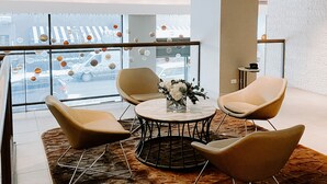 Um interior moderno com uma mesa redonda, quatro cadeiras, um vaso com flores e vista para a rua através de grandes janelas.