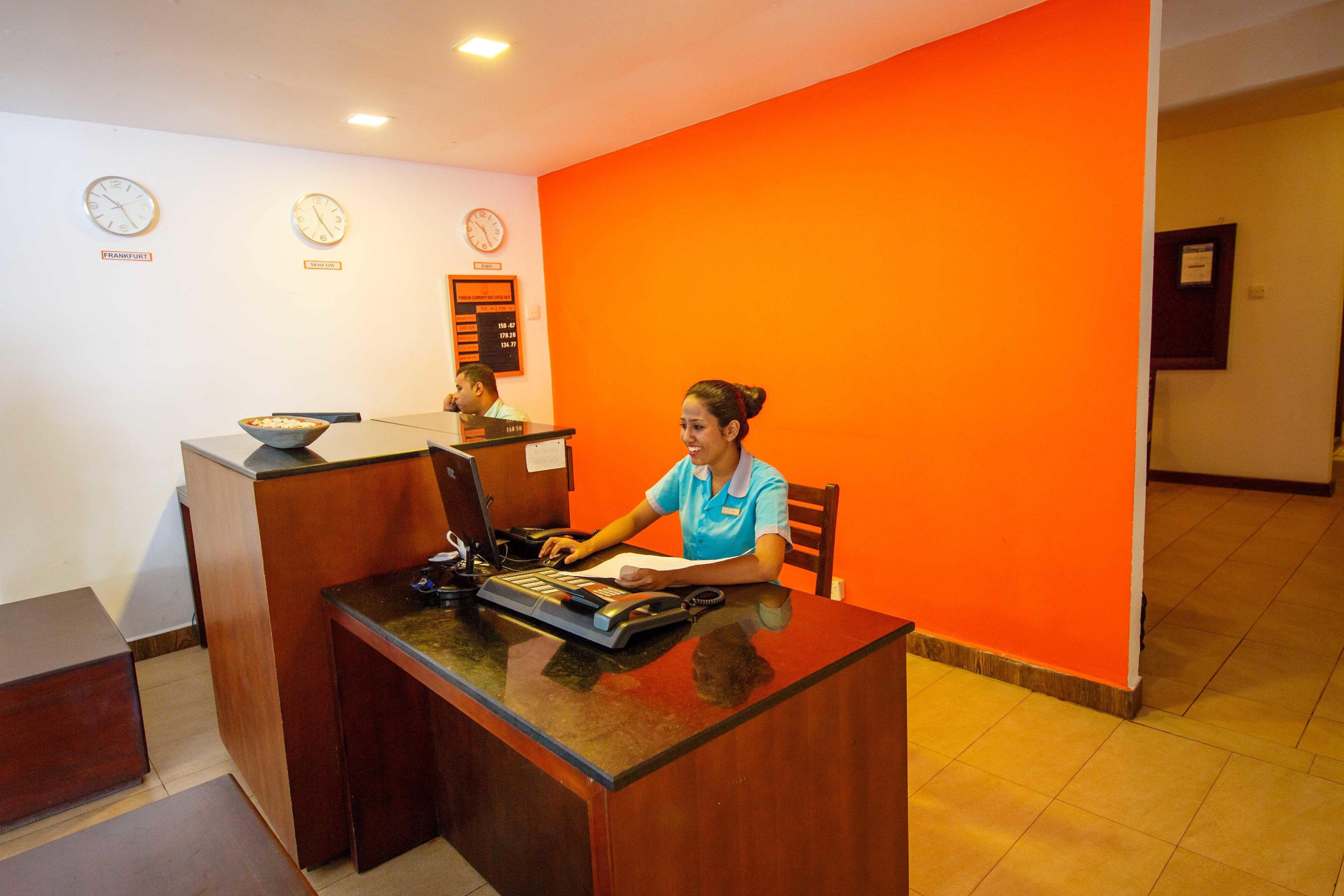 Bancada de recepção com um computador, um relógio e uma placa indicando a hora.