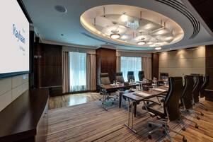 Uma sala de conferências com uma mesa comprida, várias cadeiras e uma tela de projetor exibindo "Rayhaan by Wihara Dubai".