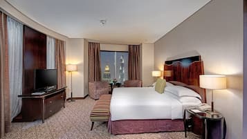 Quarto de hotel com uma cama grande, televisão, escrivaninha e vista para um prédio alto.