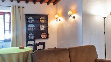 Quarto aconchegante com teto de madeira, sofá marrom, mesa de jantar com toalha verde e pratos decorativos na parede.