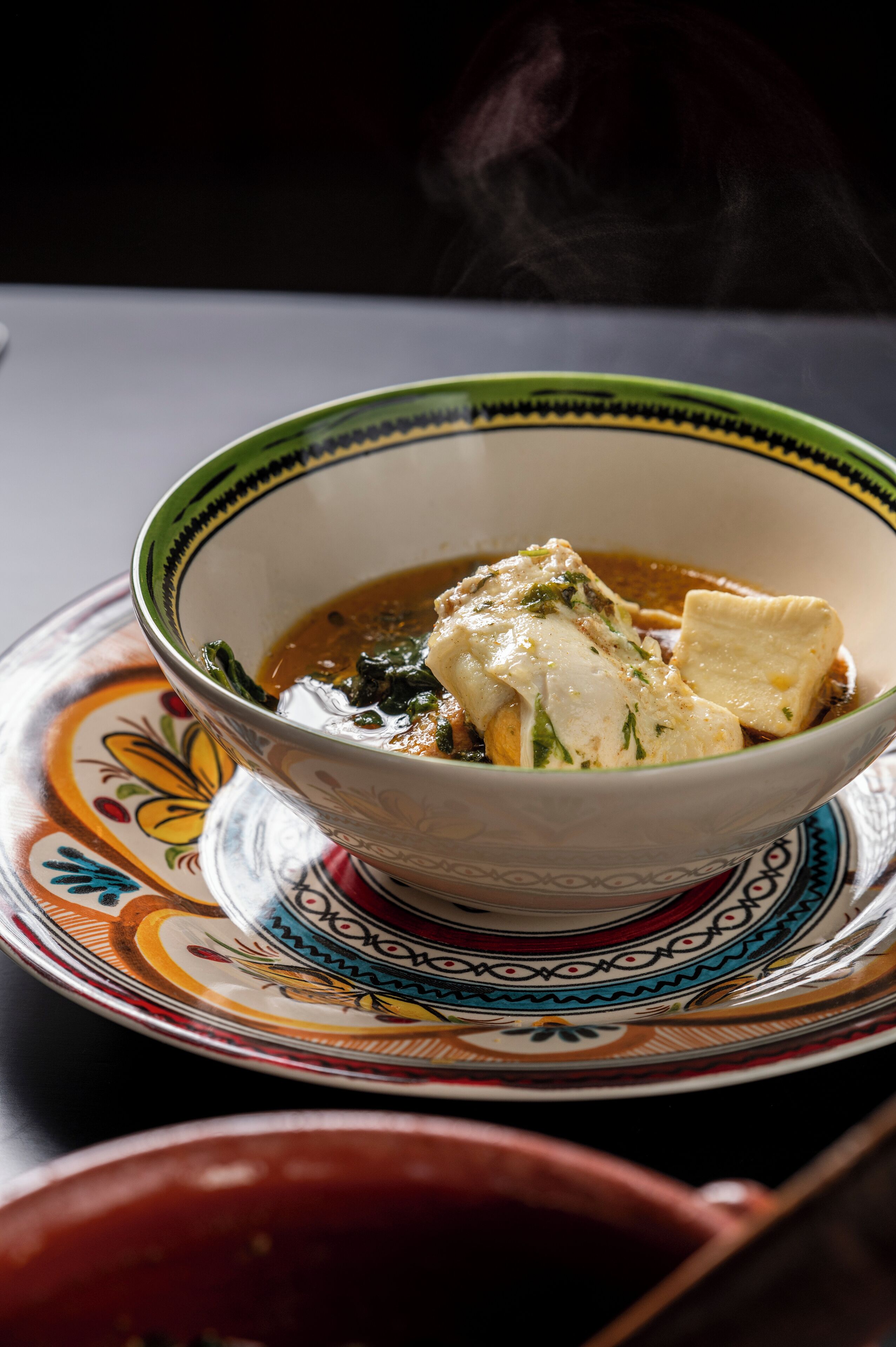Uma tigela de sopa com um prato decorativo embaixo.