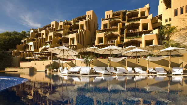 Um hotel com área de piscina, incluindo espreguiçadeiras e guarda-sóis, rodeado por edifícios altos com um estilo arquitetônico singular.