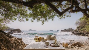 Mesa posta numa praia rochosa, com vista para o oceano e ilhas ao longe.