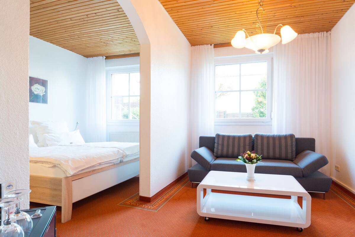 Quarto com cama, sofá, mesa de centro e janela com cortinas.