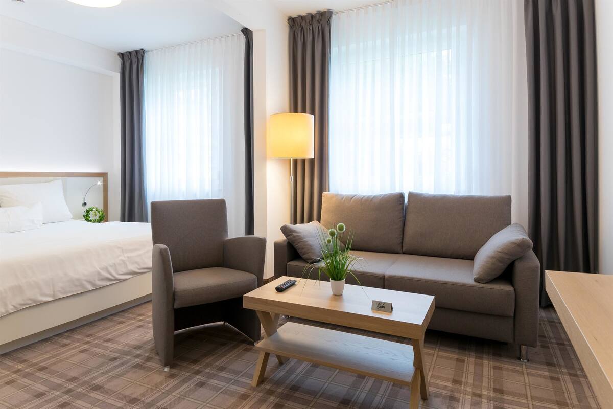 Quarto de hotel com cama, sofá, mesa de centro e abajur.