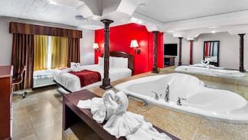 Quarto de hotel com cama grande, área de estar, pia dupla e espelho amplo.