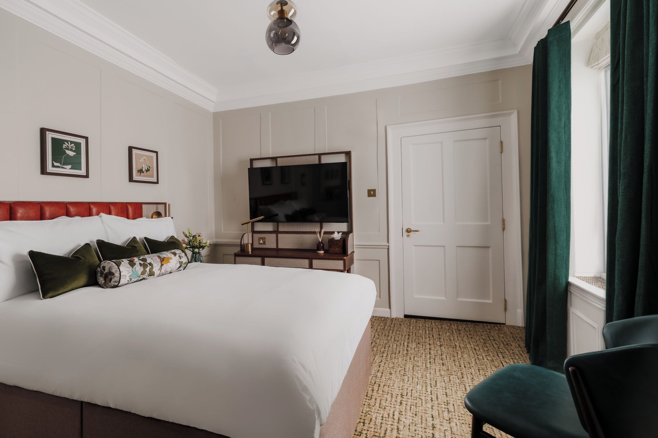 Quarto de hotel com uma cama grande, televisão, escrivaninha e uma cadeira.