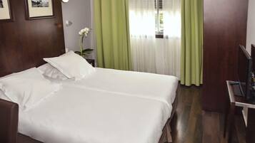 Quarto de hotel com cama de casal, uma mesa de escritório com computador e janela com cortinas verdes.