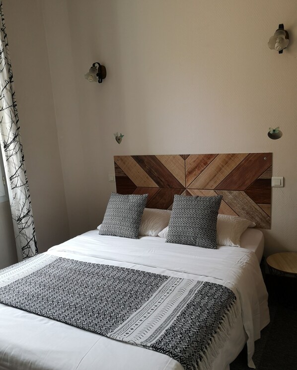 Uma cama bem arrumada com roupa de cama estampada, uma cabeceira de madeira geométrica e uma pequena mesa de cabeceira com abajur.