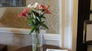 Um vaso com flores sobre uma mesa em um quarto com papel de parede estampado e quadros nas paredes.