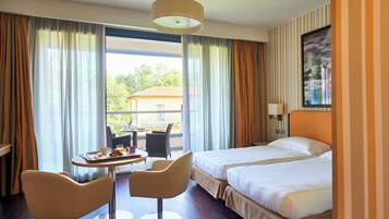 Quarto de hotel com duas camas, uma mesa de jantar com cadeiras, vista para o exterior e um quadro na parede.