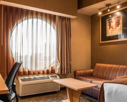 Quarto de hotel com uma janela grande, um sofá, uma mesinha e uma escrivaninha com cadeira.