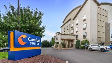 Entrada de hotel com placa da Comfort Suites, estacionamento e um edifício com várias janelas.
