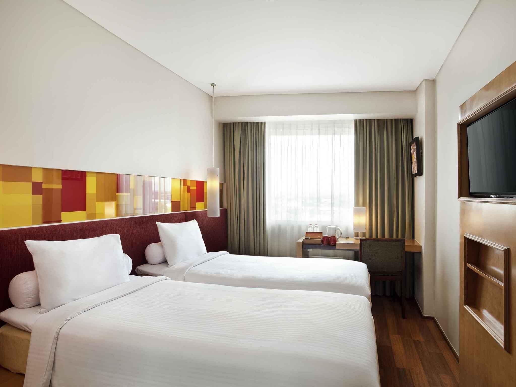 Quarto de hotel com duas camas, uma mesa, televisão e janela com cortinas.