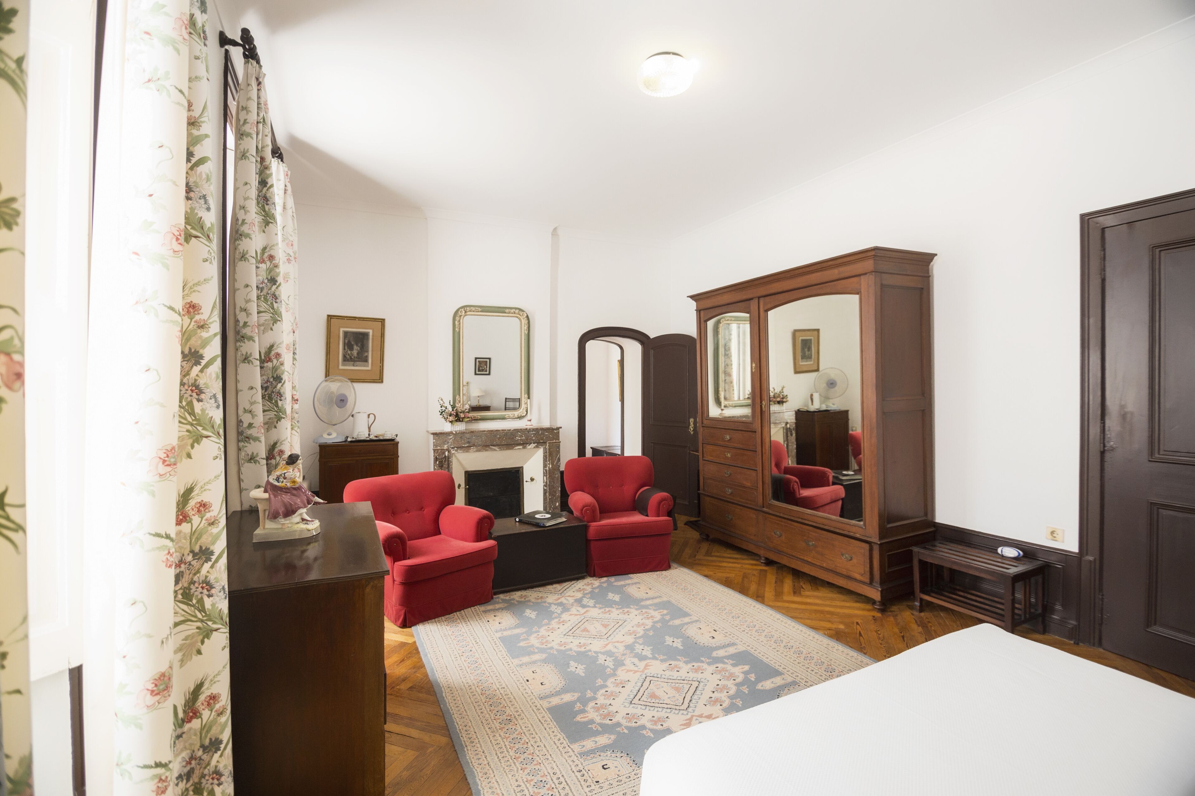 Quarto com cama, poltronas vermelhas, guarda-roupa de madeira, espelho e lareira.