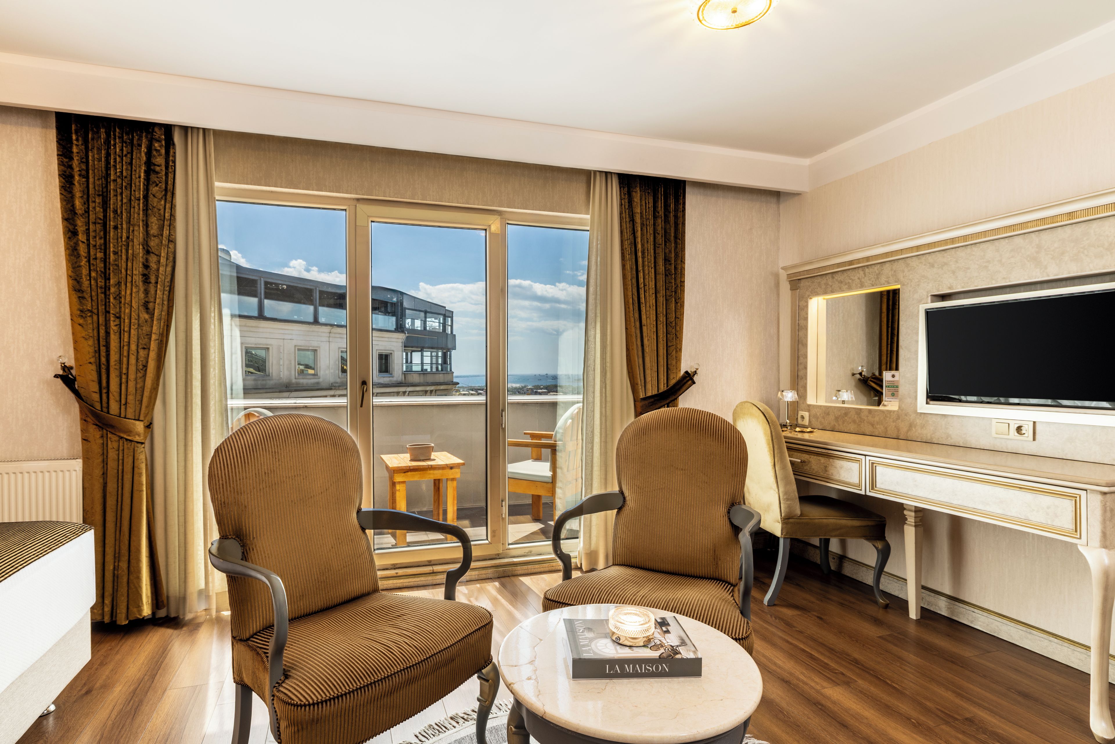 Quarto de hotel com varanda, duas poltronas, uma mesinha, televisão e minibar.
