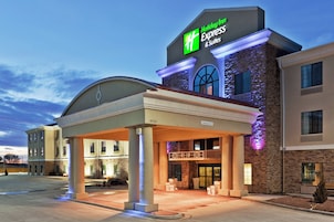 Um hotel Holiday Inn Express & Suites com entrada coberta, fachada de pedra e letreiros iluminados.