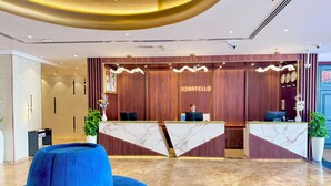 Uma área de recepção de hotel com balcões de mármore, um recepcionista e uma cadeira azul.