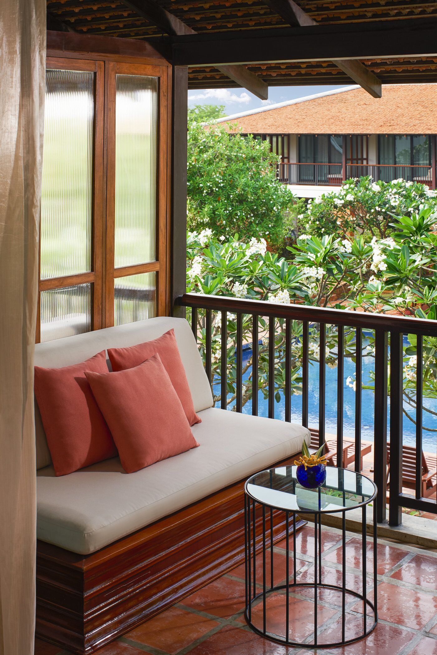 Varanda com sofá e mesa pequena, com vista para um jardim e um prédio.
