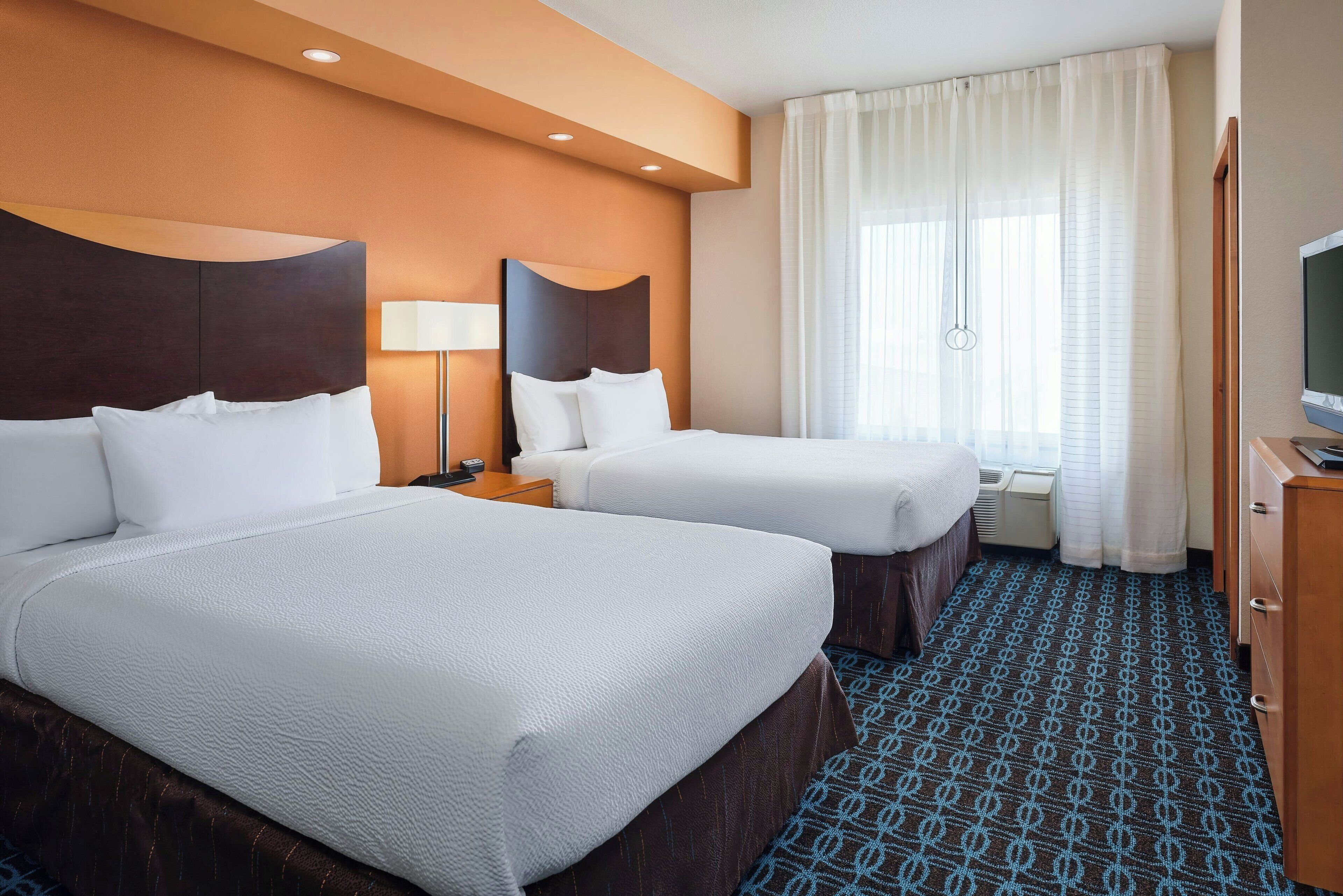 Quarto de hotel com duas camas, televisão, mesa de escritório e janela com cortinas.