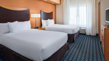 Quarto de hotel com duas camas, televisão, mesa de escritório e janela com cortinas.