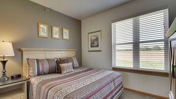 Quarto com cama, mesa de cabeceira, abajur e janela com persianas.
