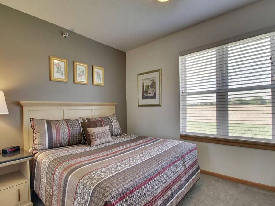 Quarto com cama, mesa de cabeceira, abajur e janela com persianas.