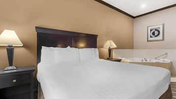 Quarto de hotel com uma cama grande, duas luminárias de cabeceira, mesa de cabeceira, banheiro com banheira e uma moldura com uma imagem na parede.
