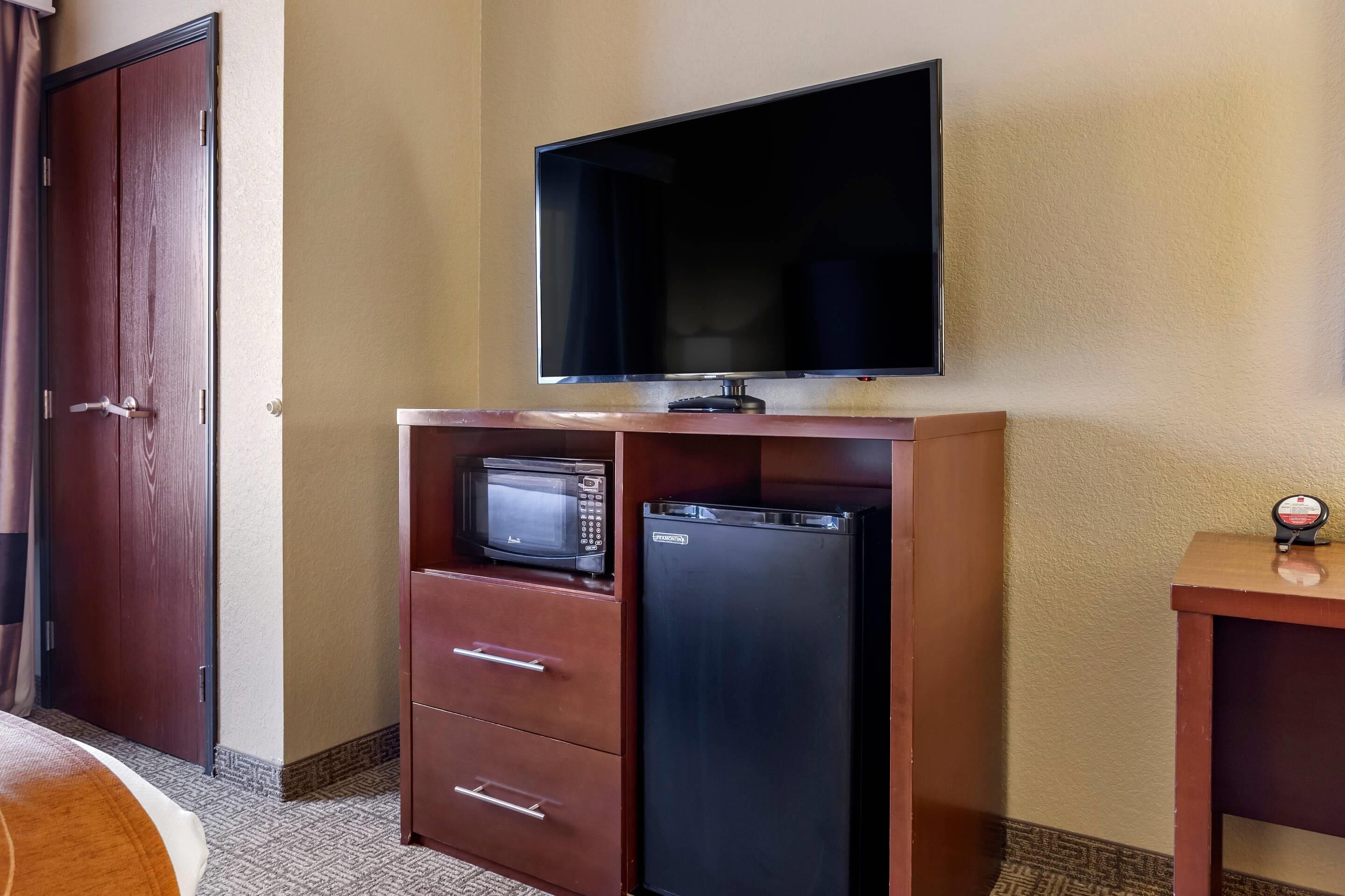 Quarto de hotel com armário de madeira contendo micro-ondas, geladeira e televisão de tela plana.