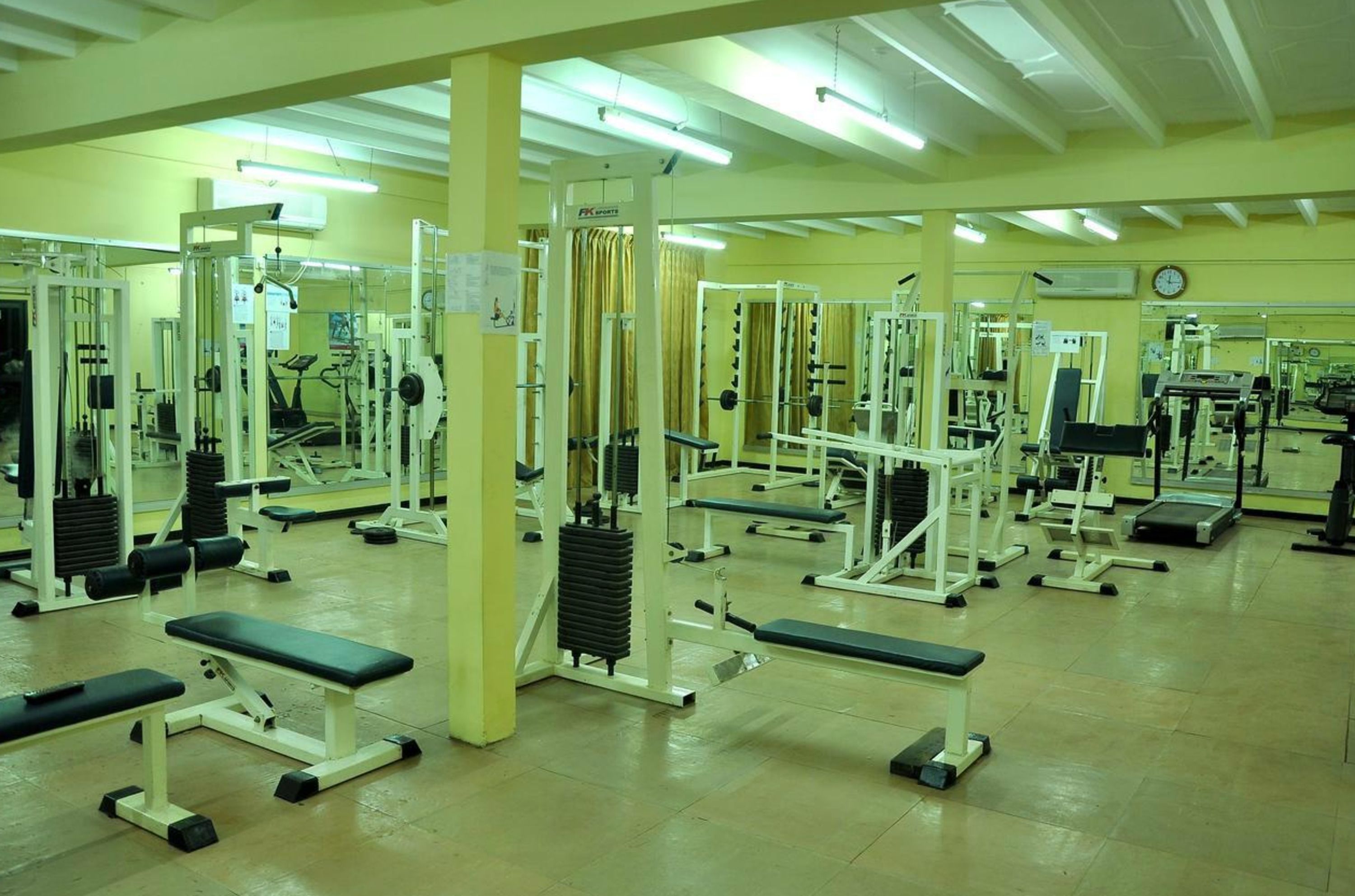 Uma academia com diversos equipamentos de ginástica, espelhos e bancos.