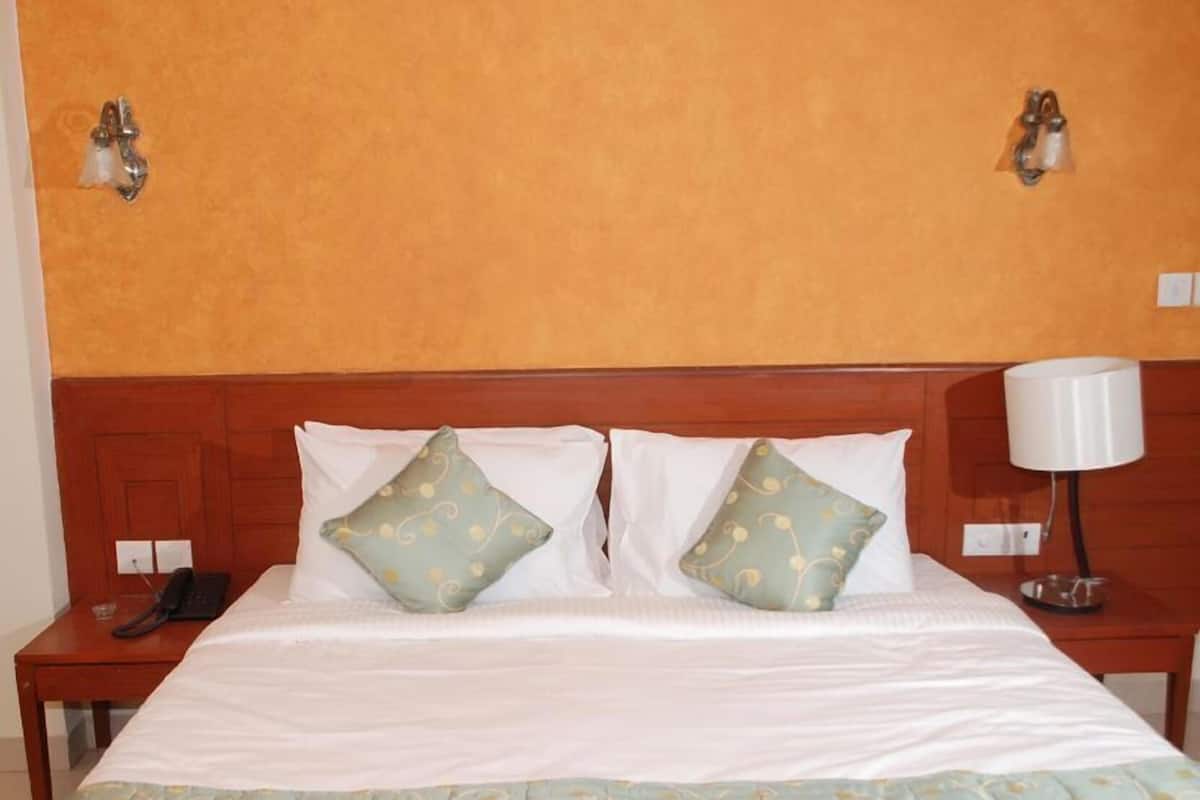 Quarto de hotel com cama, duas mesas de cabeceira, abajur e telefone.