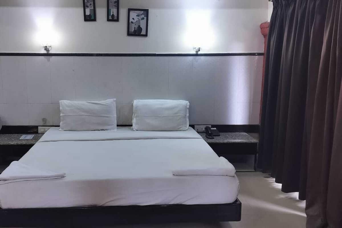 Quarto de hotel com cama, duas mesas de cabeceira, um criado-mudo, um sofá e uma janela com cortinas.