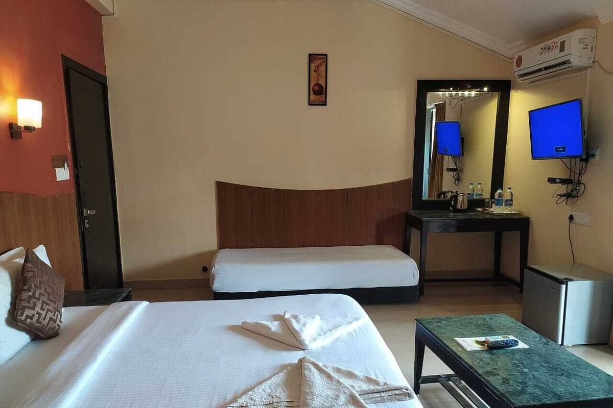 Quarto de hotel com duas camas, uma escrivaninha, um espelho e uma televisão.