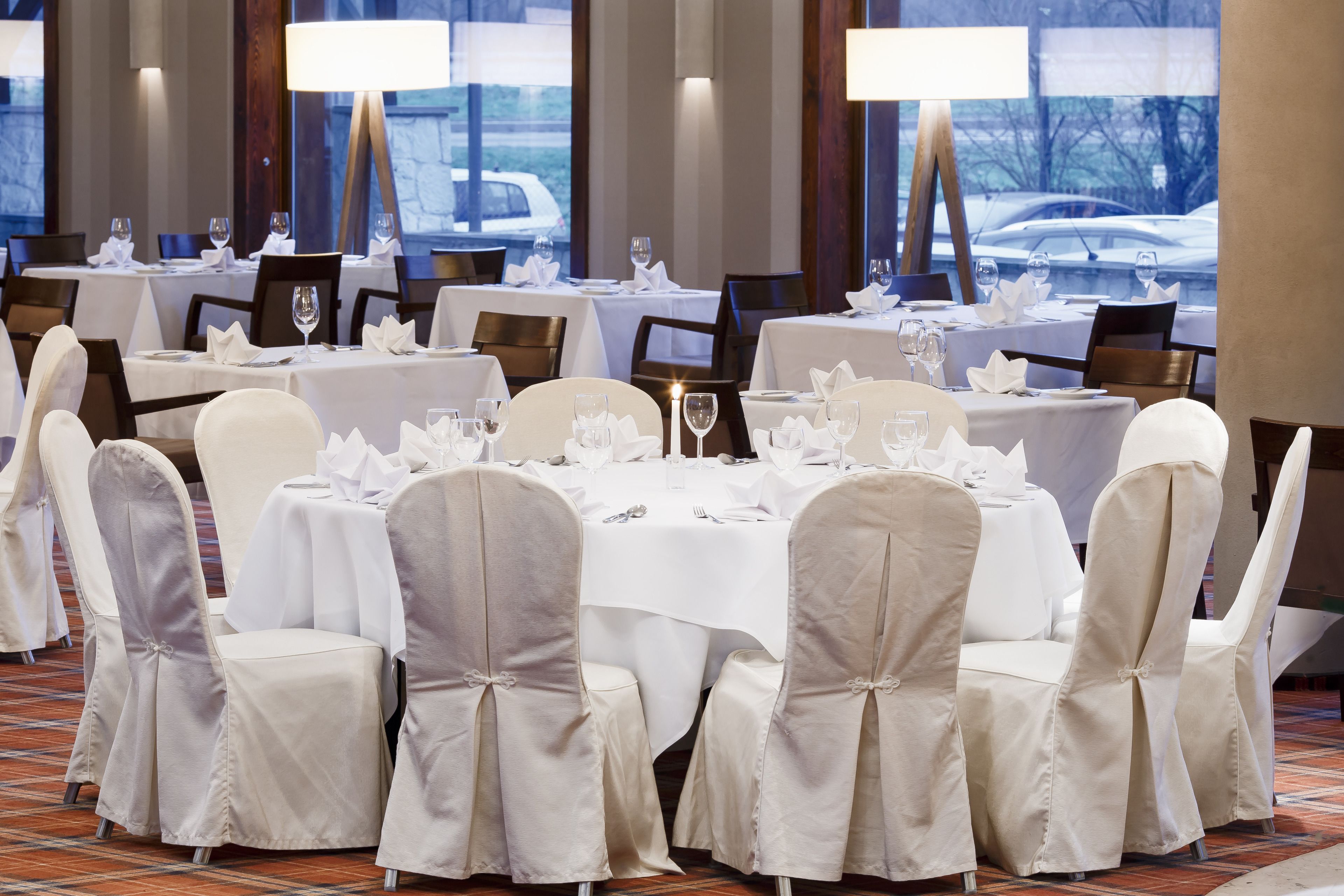 Uma sala de banquetes com mesas redondas preparadas para refeições, cada uma com toalhas brancas e copos.