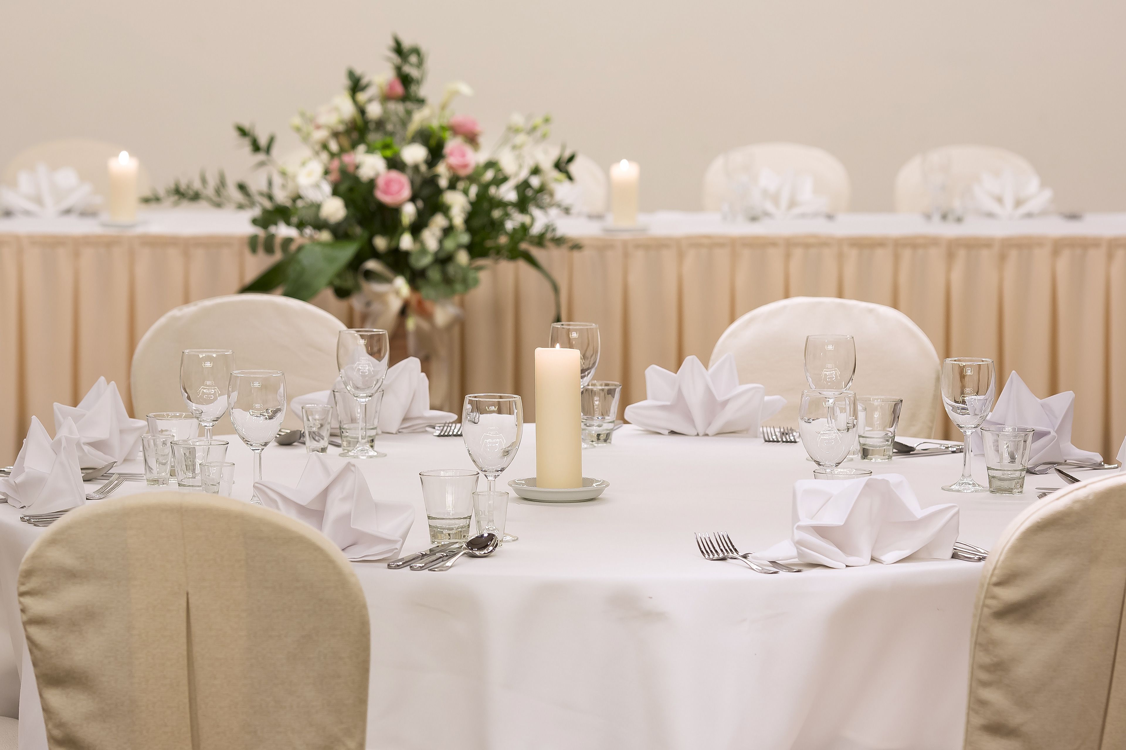 Mesa de jantar formal posta com toalhas brancas, velas e arranjos florais.