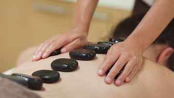 Sessão de massagem com uma pessoa de bruços recebendo pressão das mãos de um terapeuta em uma mesa de massagem.