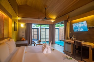 Quarto de hotel com uma cama, escrivaninha, televisão e varanda com cortinas.
