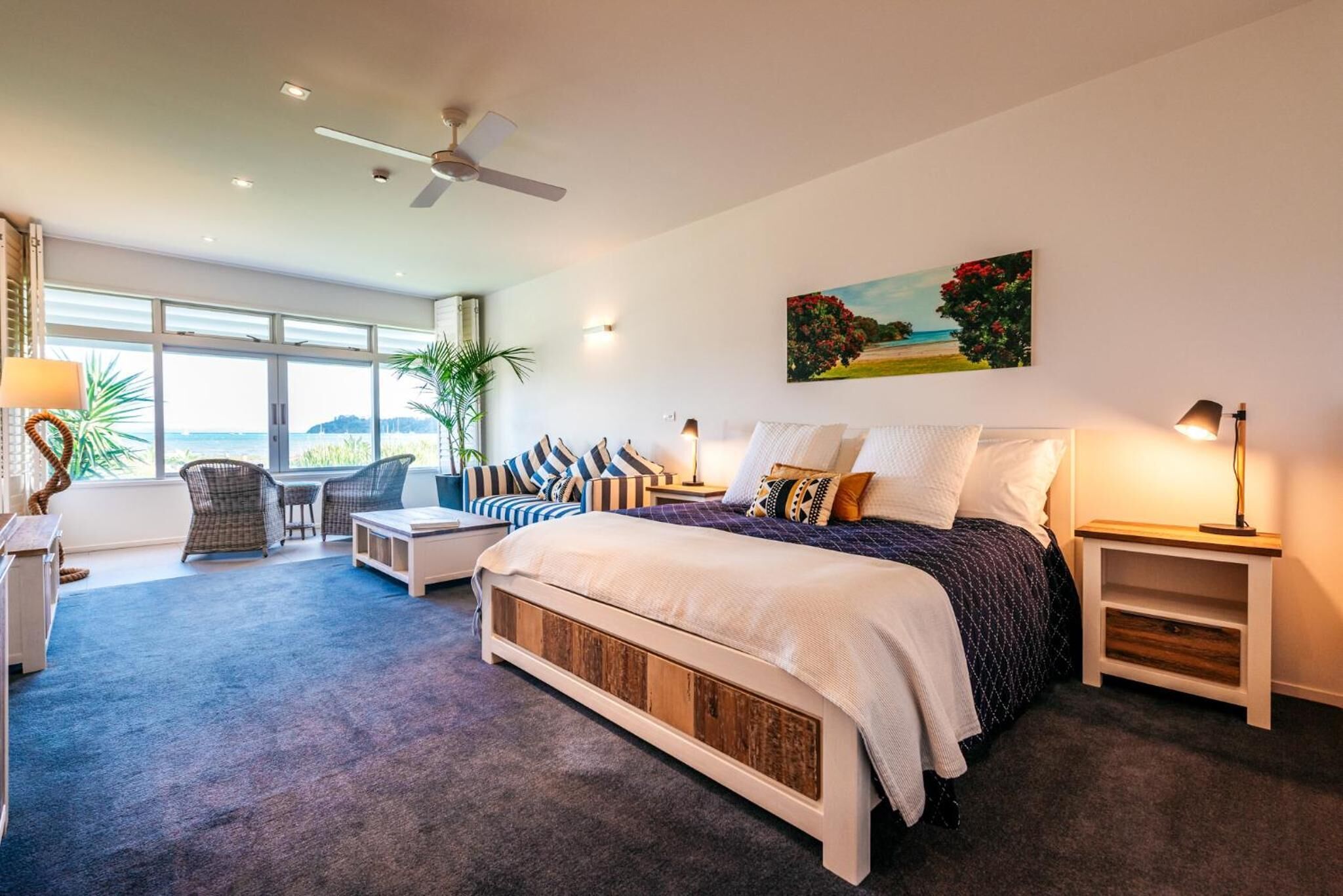 Quarto com uma cama grande, área de estar com vista e ventilador de teto.