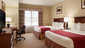 Quarto de hotel com duas camas, uma escrivaninha com computador, uma cadeira e uma janela com cortinas.