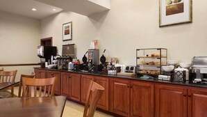 Uma mesa de pequeno-almoço com armários de madeira, uma máquina de café e diversos itens para o pequeno-almoço.