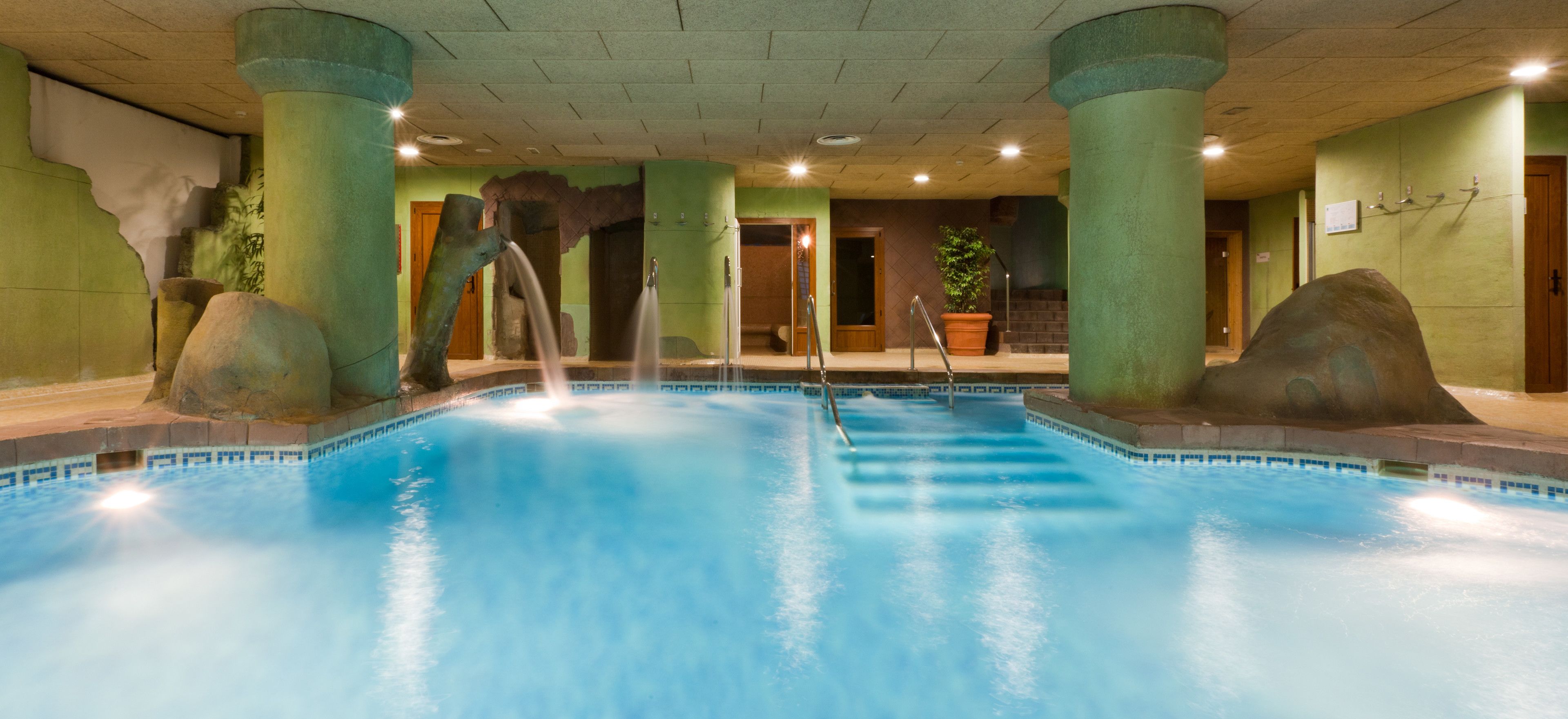 Piscina interior com água cristalina, rodeada por pilares de pedra e borda revestida de azulejos.