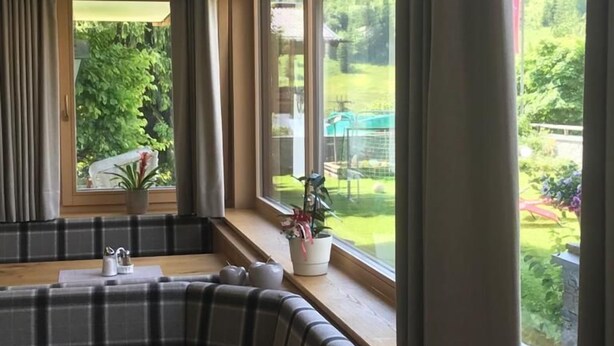 Uma sala de estar moderna com uma janela grande, um sofá, uma mesa de madeira e uma planta em vaso.