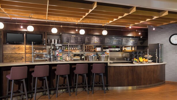 Uma área de bar moderna com teto de madeira, banquetas, balcão com cardápio e um relógio na parede.